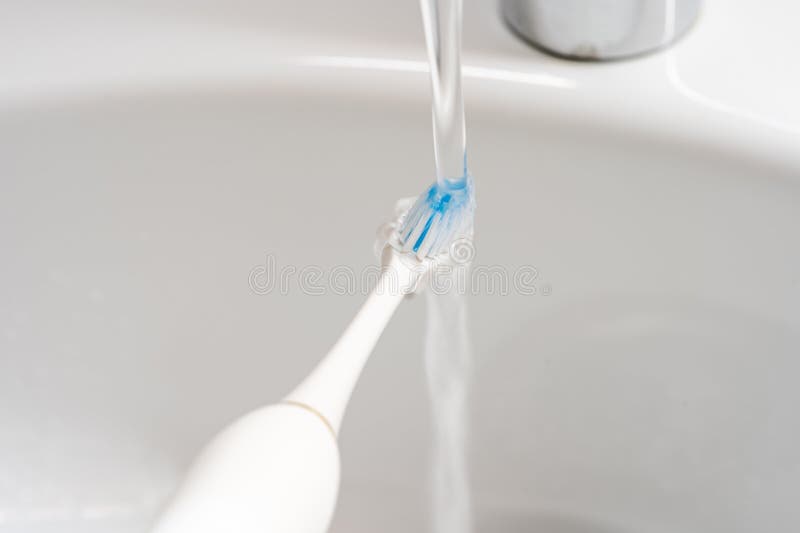 A Toothbrush Under a Running Water Stream in a White Sink Stock Photo ...