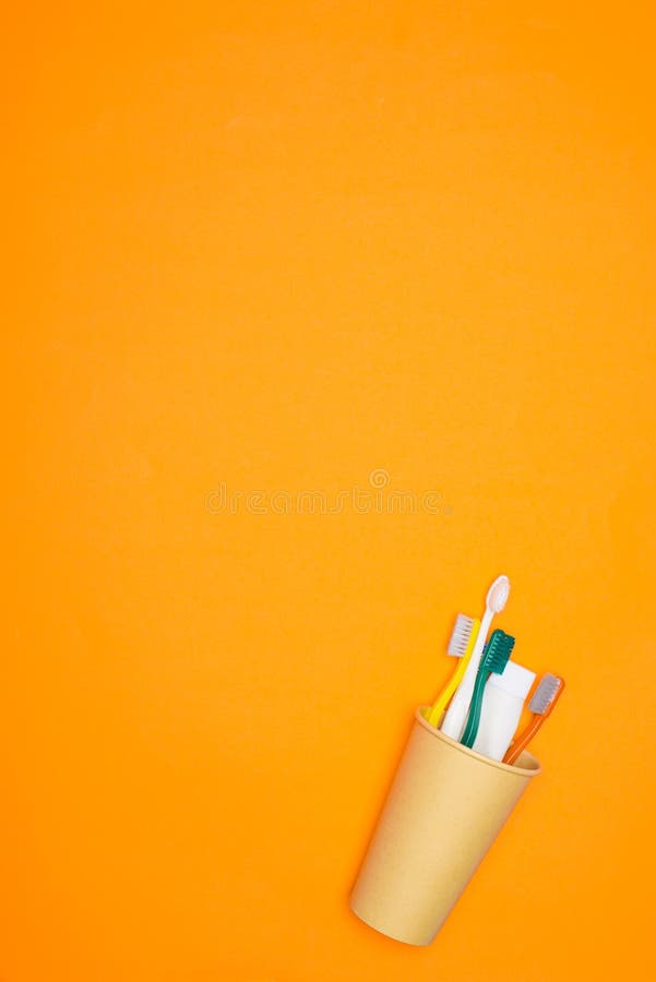 Toothbrushes and Toothpaste in Paper Cup, Isolated on Orange Stock ...