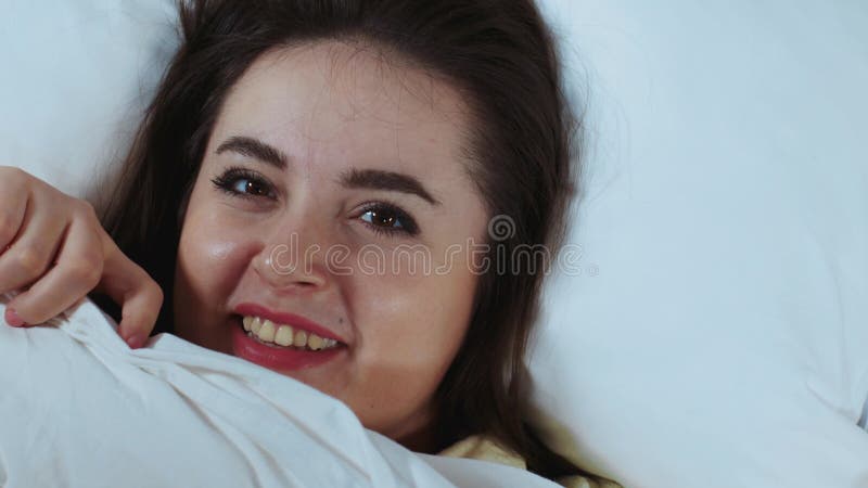 Top View Of A Cheerful Young Woman Hiding Under A Soft White Blanket