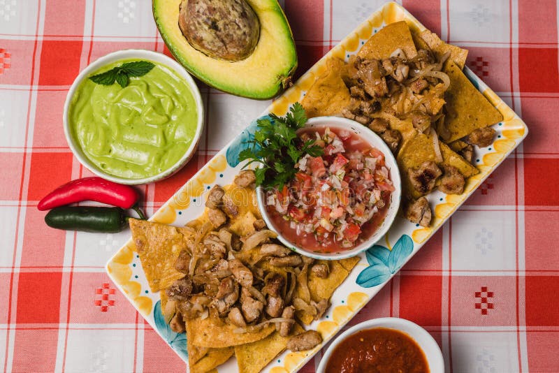 Top View of a Plate of Beef Nachos Next To Dips and Avocado, on a Red ...