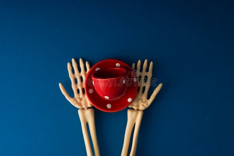 Top View of Skeleton Hands Holding a Red Cup on a Saucer Against a Blue ...
