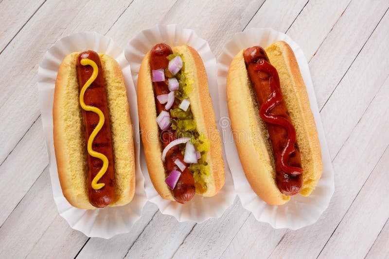 Three Hot Dogs on a Wood Table with Different Condiments Stock Image ...