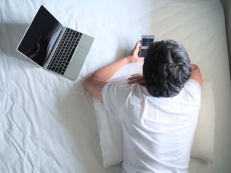 Top View of Young Man Using Phone and Laptop on the Bed in Bedroom ...