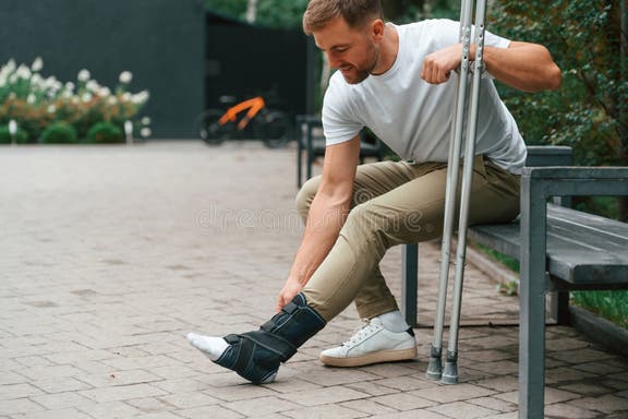 Touching the Leg. Man with Crutches is in the Park Outdoors Stock Image ...
