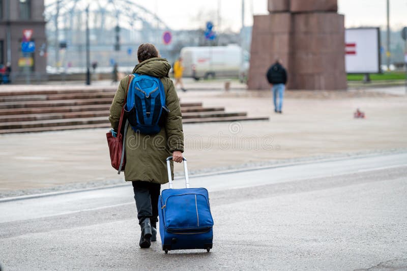 A Tourist with a Backpack Pulls a Suitcase on Wheels Down the Street ...