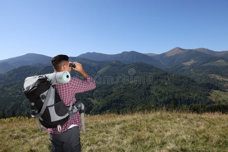 Tourist with Hiking Equipment Looking through Binoculars in Mountains ...