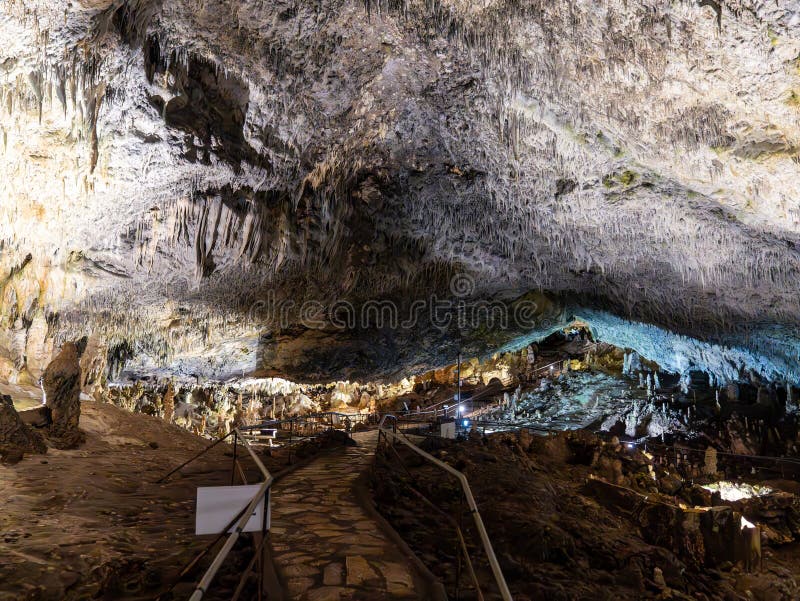 Tourists Walking on Path Inside Illuminated Cave with Stalactites and ...