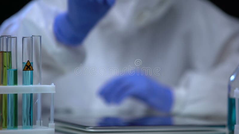 Toxic Lab Worker Examining Harmful Liquid and Making Notes on Tablet ...