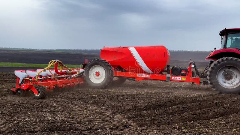 A Tractor with a Seeder Rides through the Field and Sows Wheat Grains ...
