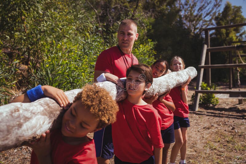 Trainer Assisting Kids in Carrying a Heavy Wooden Log during Obstacle ...