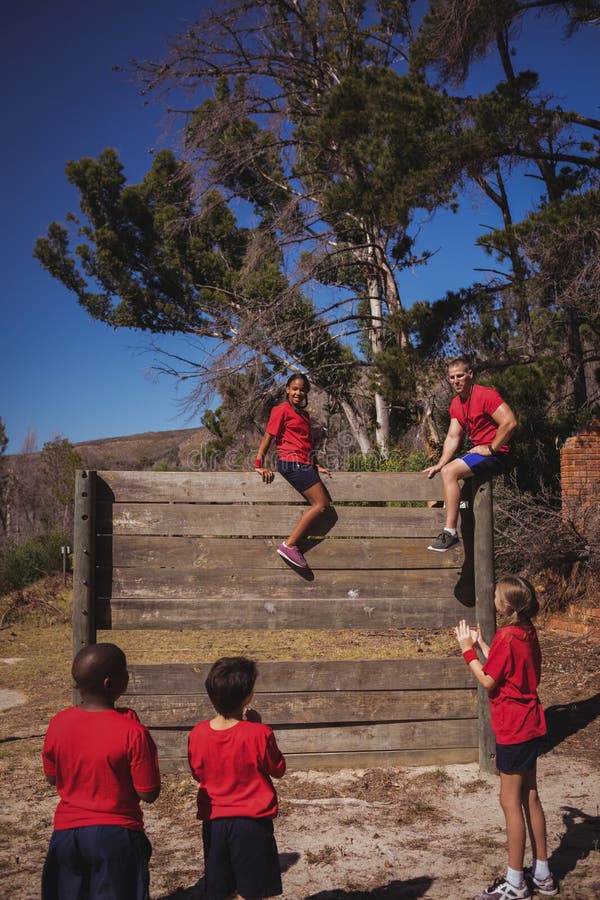 Trainer Assisting Kids To Climb a Wooden Wall during Obstacle Course ...