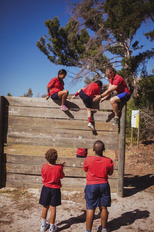 Trainer Assisting Kids To Climb a Wooden Wall during Obstacle Course ...