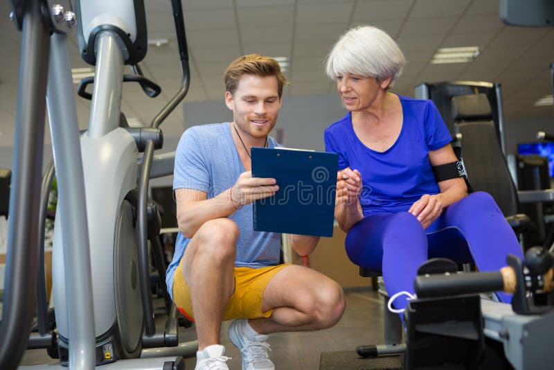 Trainer with Clipboard Helping Eldery Woman in Gym Stock Photo - Image ...