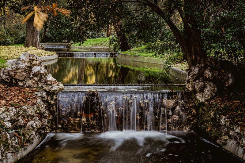 Small Waterfall Running Under Trees and Stone Benches in a Park Stock ...
