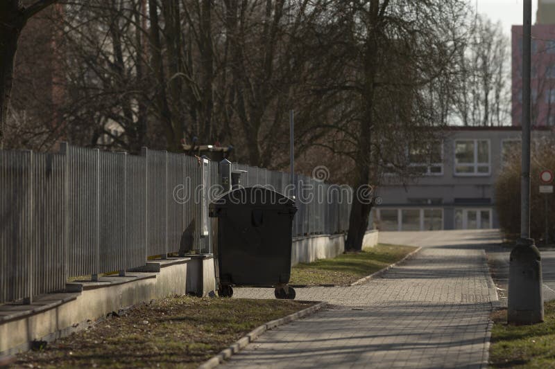 A Trash Can is Positioned on the Sidewalk beside a Fence Stock Photo ...