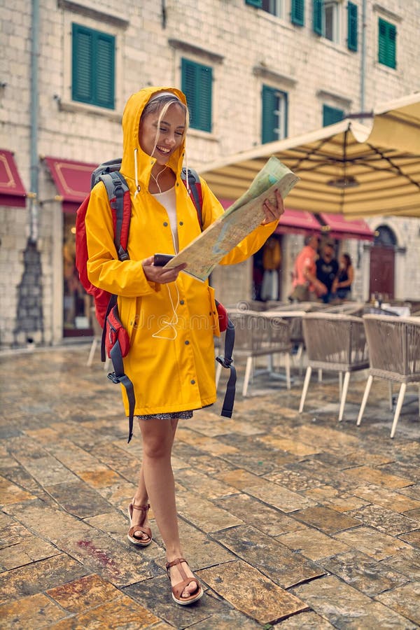 Travel Girl With A Yellow Raincoat And Map On The Street While Enjoying A Walk Through The City