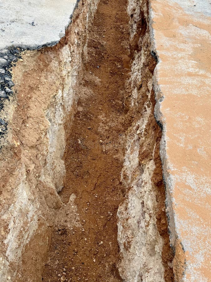 A Trench with Exposed Soil Layers. the Surrounding Concrete Road is Cut ...