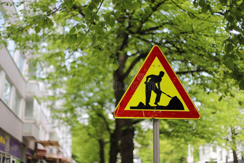 Triangle Road Construction Sign on a Post at a Street with Trees Stock ...