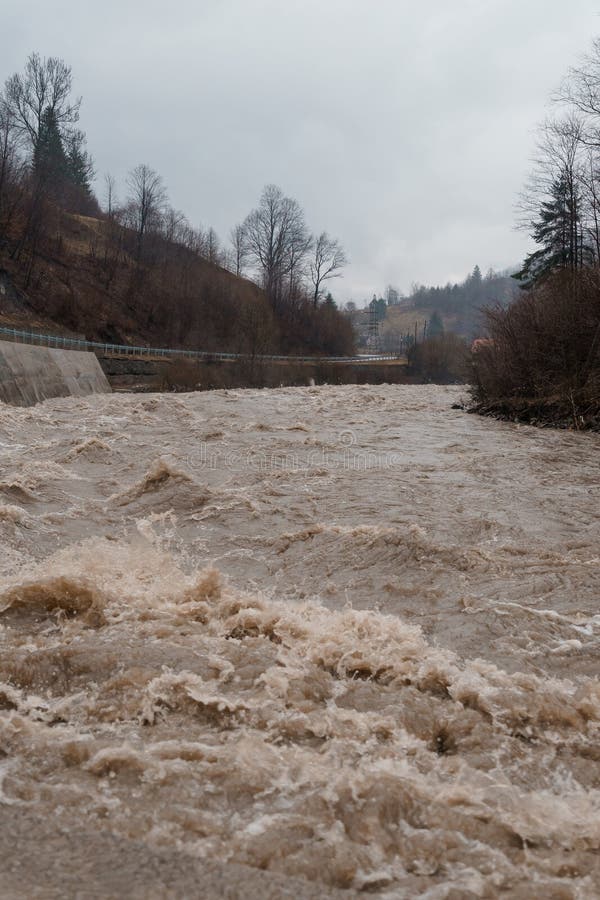 Turbulent River Flowing Under Overcast Skies Amidst Bare Trees and ...