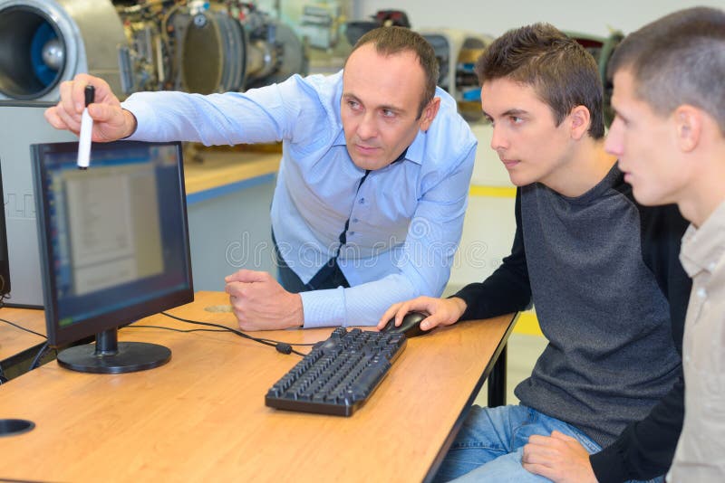 Tutor Advising Two Male Students Using Computer Stock Photo - Image of ...