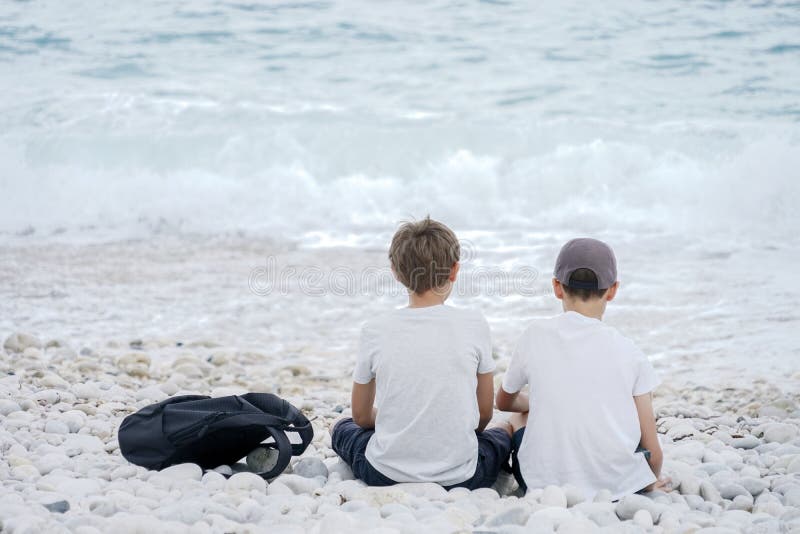Två Pojkar Som Sitter Bredvid De På Stranden Vid Havet Fotografering