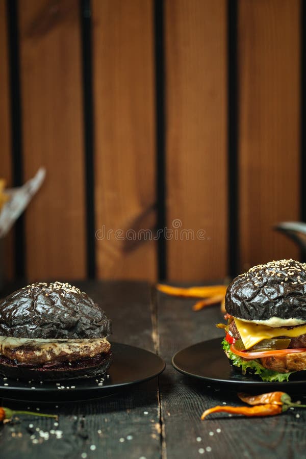 Two Appetizing Black Burgers on Black Plates on the Dark Wooden Table ...