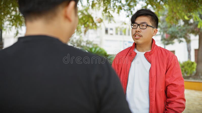 Two Asian Men Engaging in Conversation Outdoors in a City Park Stock ...