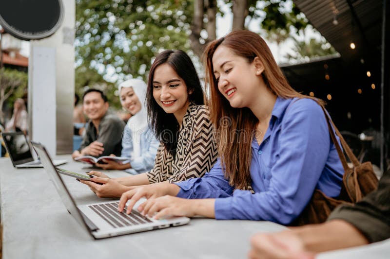 Two Beautiful University Students Studying with a Group Using a Laptop ...