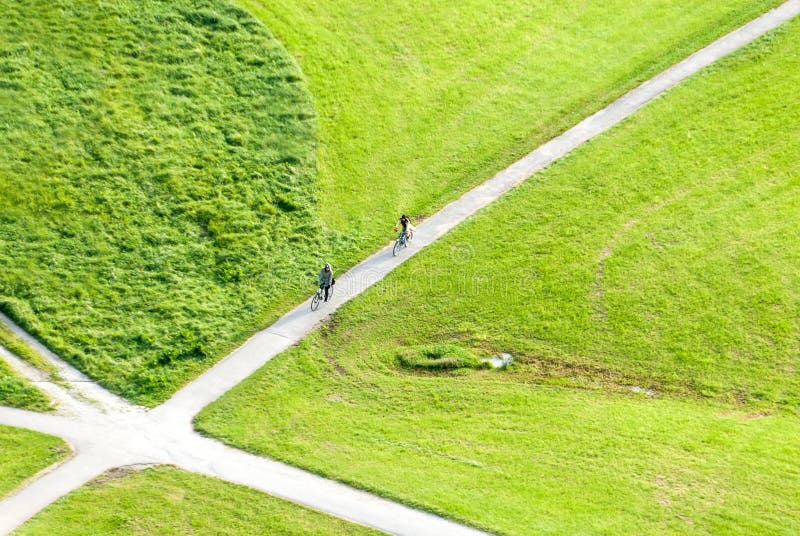 Two Bicyclists Approach a Juncture in a Green Field Stock Photo - Image ...