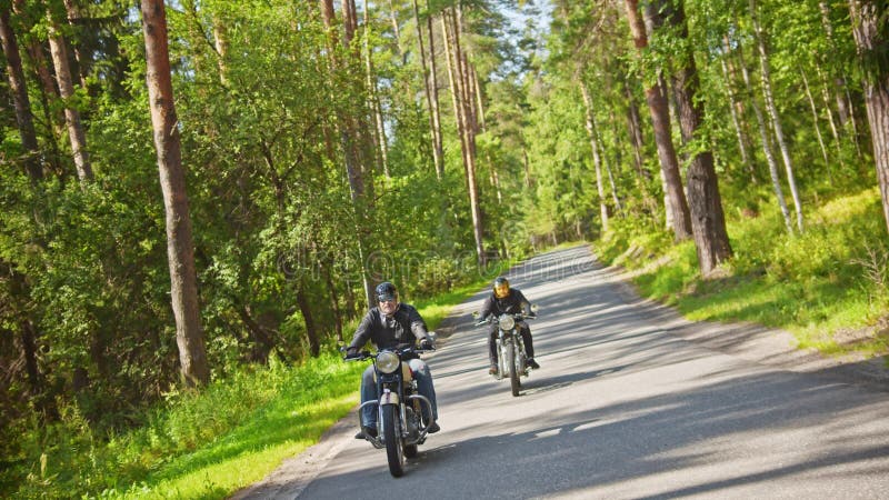 Two Bikers are Riding by Each Other Along the Road in the Green Forest ...