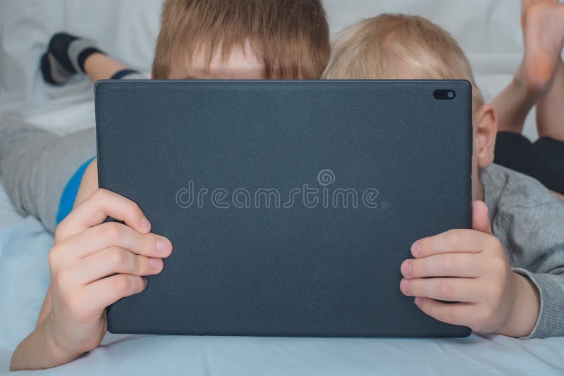 Two Boys are Lying in Bed and Looking at the Tablet. Leisure Gadgets ...