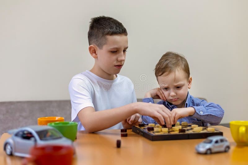 Two Boys Playing Checkers at a Table, with the Younger One Looking ...