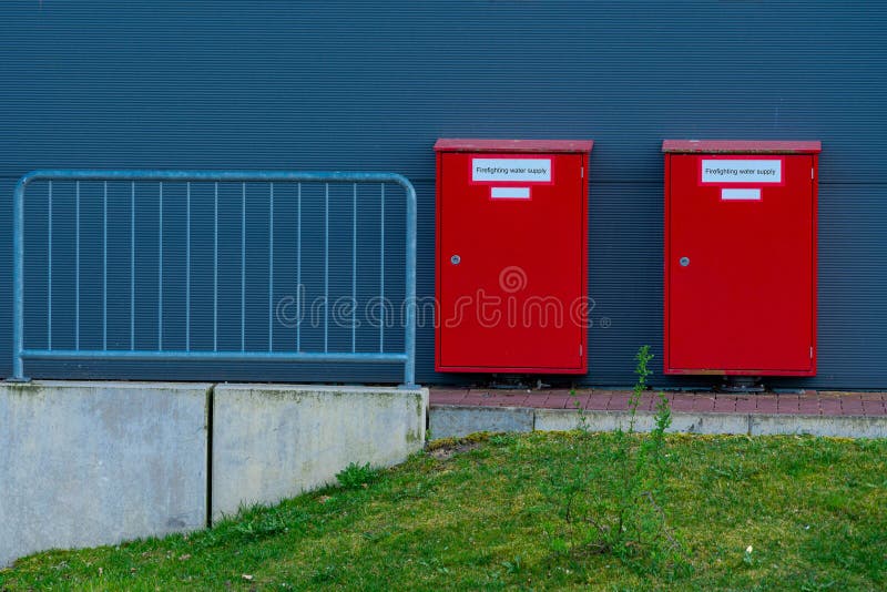Two Red Fire Boxes Next To a Gray Wall and Railing Near Green Grass ...