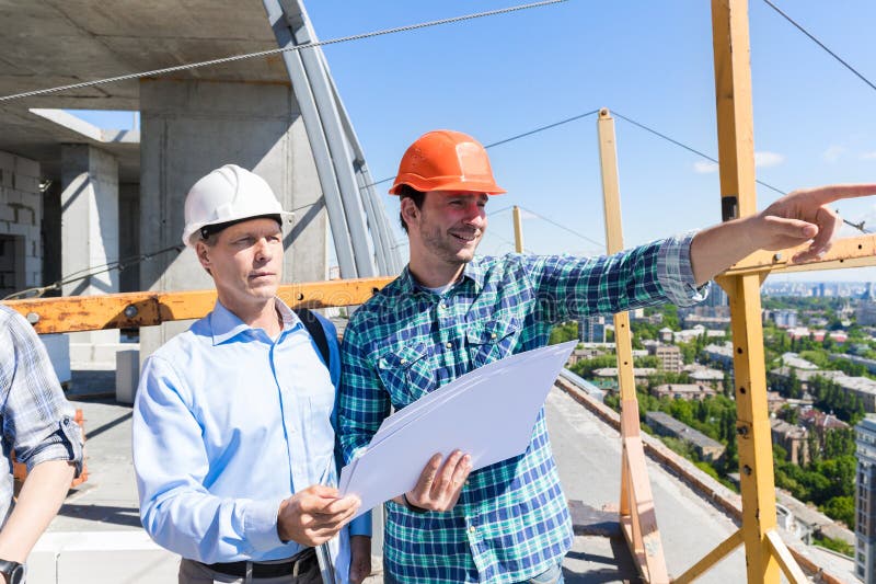 Two Builders on Construction Site Looking at Plans Contractor Meeting ...