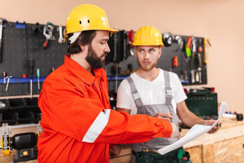 Two Builders in Work Clothes and Hardhats Working in Workshop Wi Stock ...