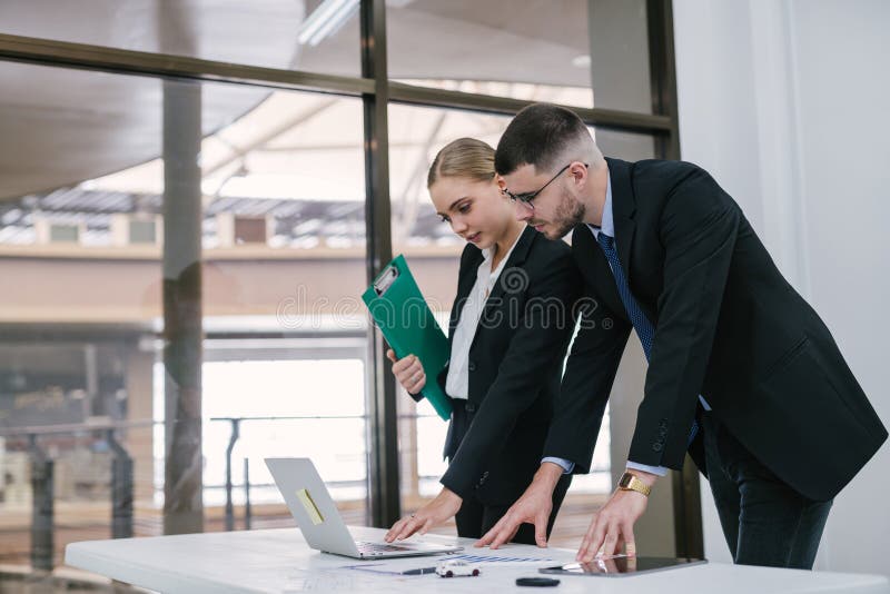 Two Business Partners Discussing Documents with a Laptop and Ideas at ...
