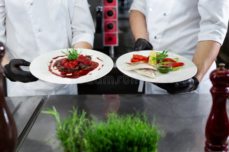 Two Chefs in a Professional Kitchen Hold Ready-made Dishes in Their ...