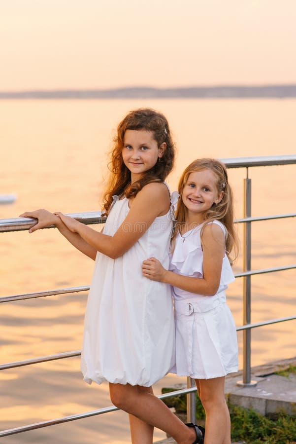 Two Child Girls are Standing on Pier by the Water, Smiling for the ... Two Child Girls are Standing on Pier by the Water, Smiling for the ...