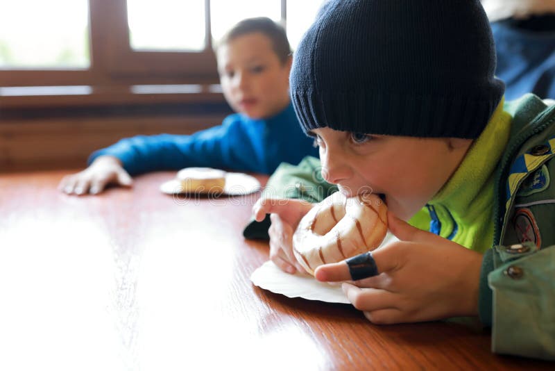 Two children eating donuts stock photo. Image of cafe - 233798650