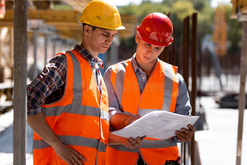 Two Civil Engineers Dressed in Orange Work Vests and Helmets Explore ...