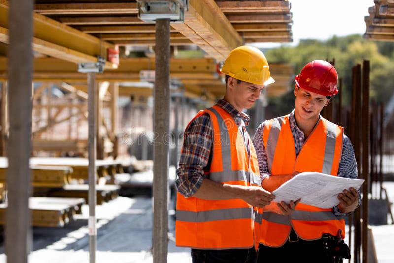 Two Civil Engineers Dressed in Orange Work Vests and Helmets Explore ...