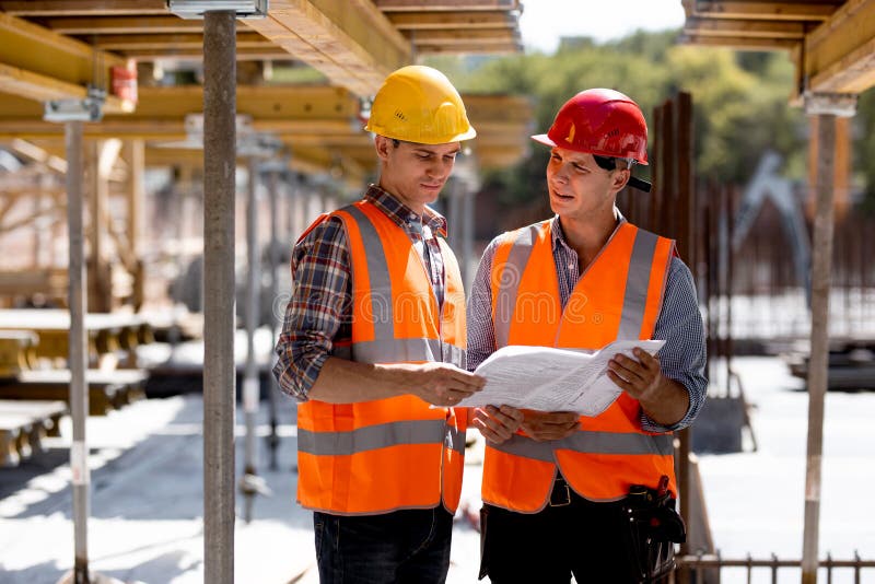 Two Civil Engineers Dressed in Orange Work Vests and Helmets Explore ...