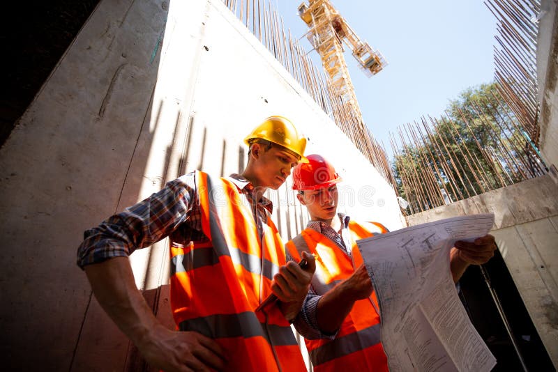 Two Civil Engineers Dressed in Orange Work Vests and Helmets Explore ...