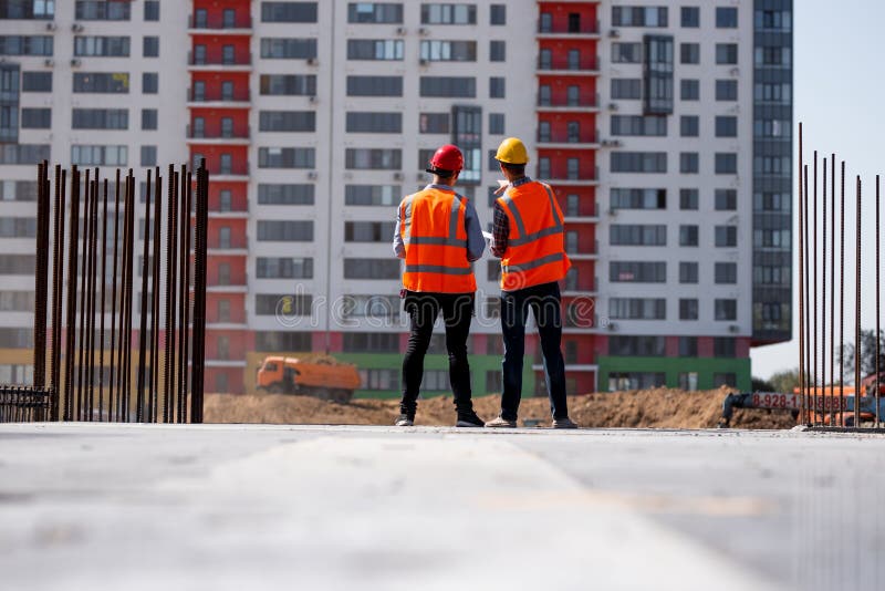 Two Civil Engineers Dressed in Orange Work Vests and Helmets Talk about ...