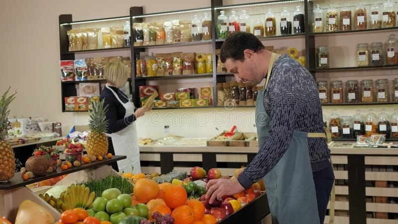 Two Clerks Work in a Grocery Store, a Man Puts Fresh Fruit on the ...