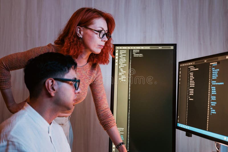 Two Colleagues Analyze Code on Dual Monitors in a Modern Office, Collaborating on Software ...