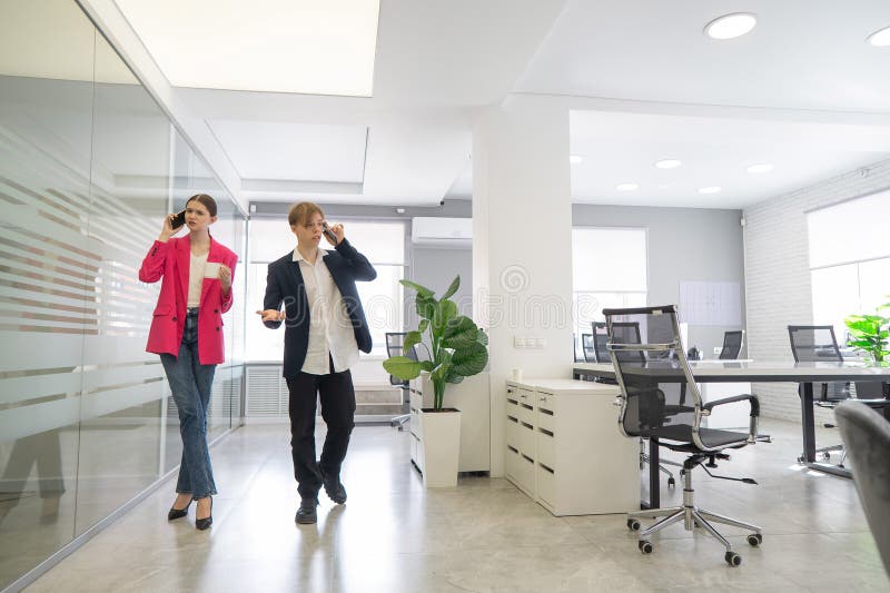 Two Colleagues are Walking through the Office and Talking on the Phones ...