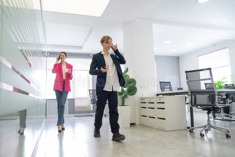 Two Colleagues are Walking through the Office and Talking on the Phones ...
