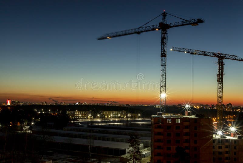 Two Construction Building Cranes Over Cityscape at Evening or Night ...