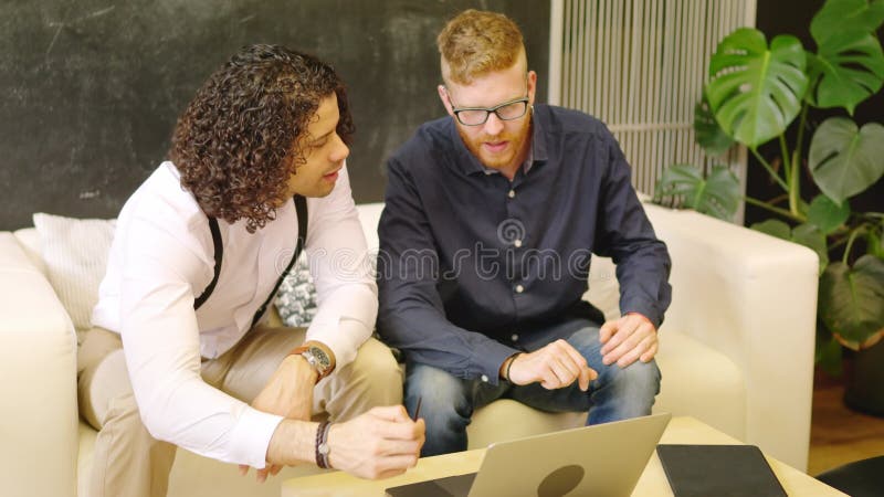 Two Coworkers Talking while Using Laptop Sitting on a Sofa Stock ...